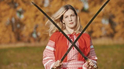 Feisty blonde woman in red national clothes standing with her swords ...