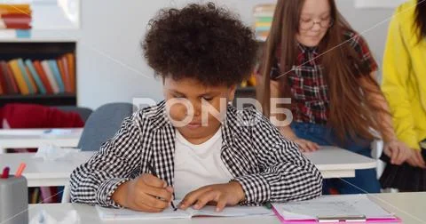 Photograph: African boy pupil writing at desk in classroom #153412602
