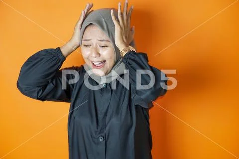 Asian woman wearing a hijab posing dizzily with both hands on her head ~ Hi Res #260681833