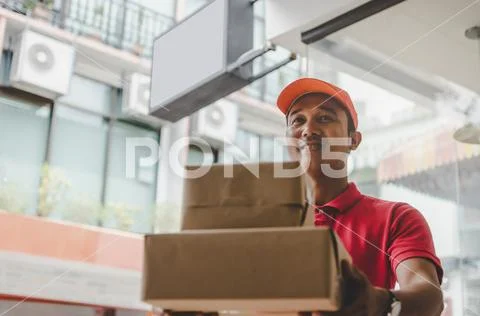 Photograph: Asian young delivery service man in red uniform sending ...