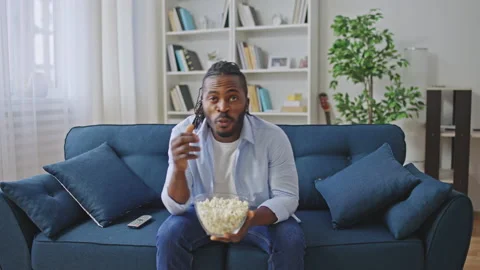 Black man eating popcorn and watching TV... | Stock Video | Pond5