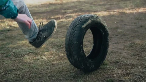 The boy kicks a tire rolling on the grou... | Stock Video | Pond5