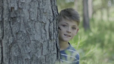 Boy peeking around tree trunk | Stock Video | Pond5
