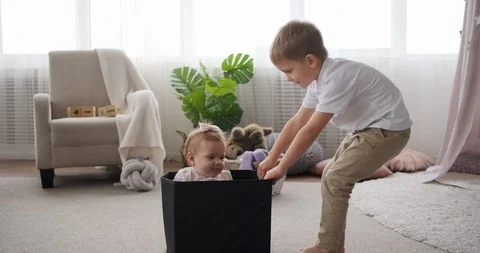 Boy pulling baby sister sitting in a box | Stock Video | Pond5