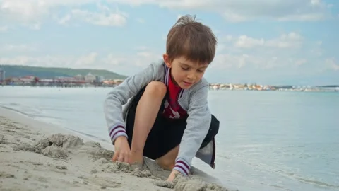 Boy sitting on the sea beach, digging an... | Stock Video | Pond5