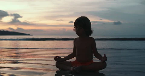 Boy sitting in yoga pose on solitude bea... | Stock Video | Pond5