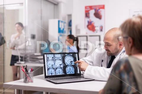 Brain surgeon pointing at ct scan on laptop ~ Premium Photo #140081879