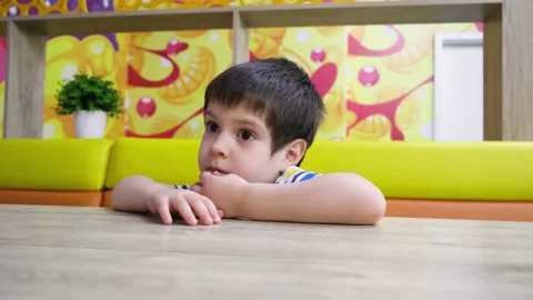 A brooding boy of 4 years sits at a tabl... | Stock Video | Pond5