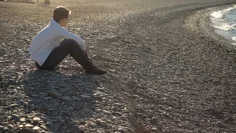 Brooding sad Teen boy sitting on the bea... | Stock Video | Pond5