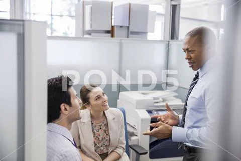 Businessman having a conversation with colleagues in office cubicle ...