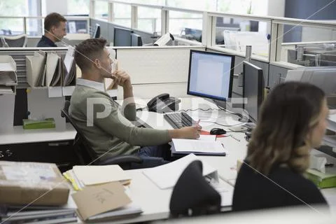 Photograph: Businessman working at computer at cubicle desk in open plan office #201768182