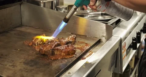 A chef uses a torch to flame broil a thi... | Stock Video | Pond5