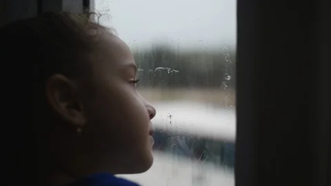 Child looks at the rain behind the windo... | Stock Video | Pond5