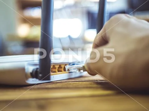 Close up hand inserting ethernet wire in wi-fi router on wooden table ...