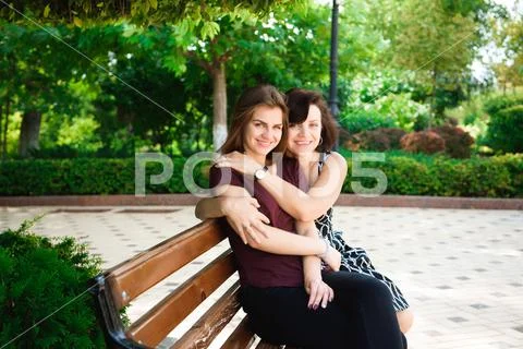 Close up portrait of mother and daughter hugging on a bench in the park Stock Photo #150560665