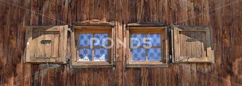 Close on two little windows on a wooden facade of old alpine chalet ...