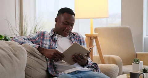 Confused man reading a book on sofa at h... | Stock Video | Pond5