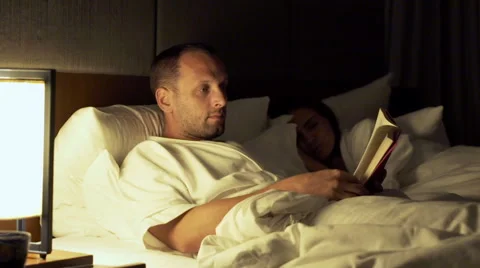Couple in bed at night, man reading book... | Stock Video | Pond5