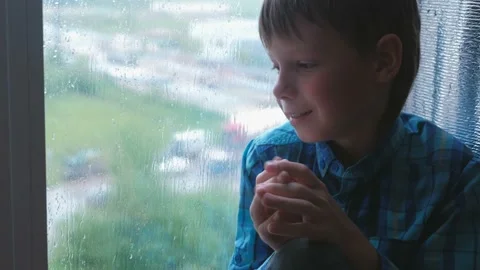 Crying boy looks out the window in the r... | Stock Video | Pond5