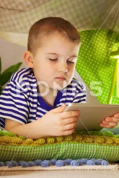 Cute boy, playing on tablet and telephone in campside, in the tent ...