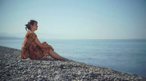 Cute girl sitting on the beach in a sad ... | Stock Video | Pond5