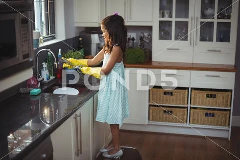 Cute little girl washing utensil in kitchen sink ~ Premium Photo #76658044