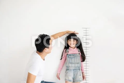Dad measures height increase of her child daughter at white brick wall ...