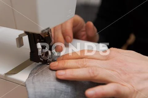 Detail of sewing machine with human hands sewing together two pieces of ...