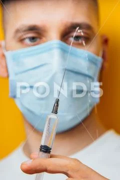 A doctor holds a syringe with a medicinal viral vaccine. Young guy in a ...