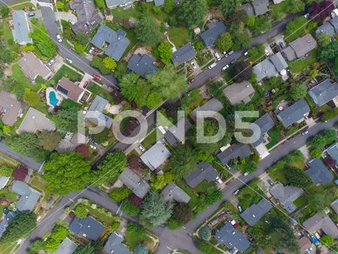 Drone shot. Small town, suburb. Lots of greenery, paved roads, roofs of ...