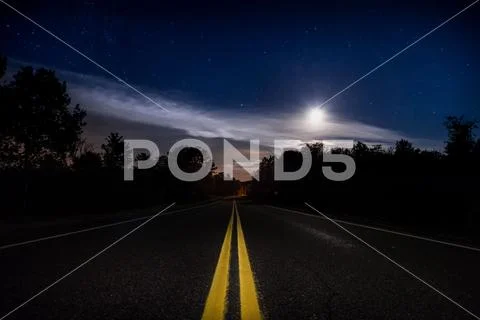 A empty road at night with the moon shining in the background ...