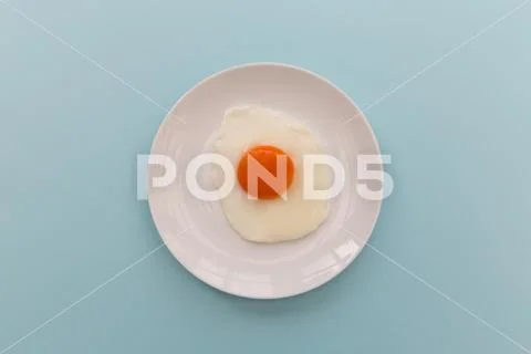 Photograph: Fried egg and yoke overhead on plate and blue background ...