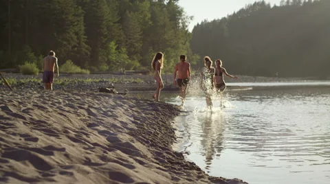 Friends run down the beach of a lake dur... | Stock Video | Pond5