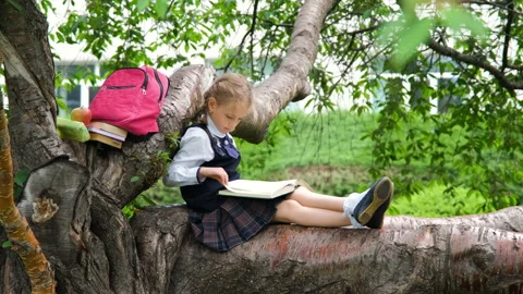 Girl in school uniform reading on tree b... | Stock Video | Pond5