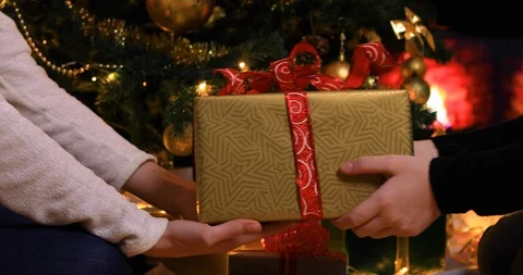 Giving a gift in front of Christmas tree... | Stock Video | Pond5