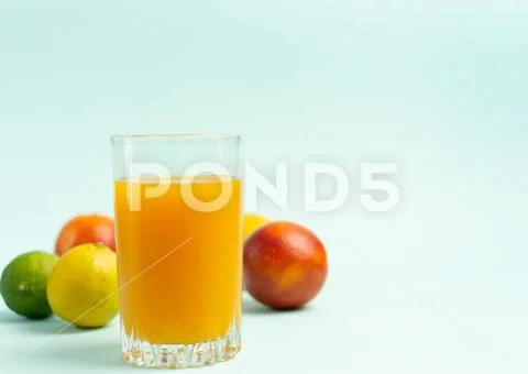 Glass of yellow juice with fruits on a blue background ~ Hi Res #150938273