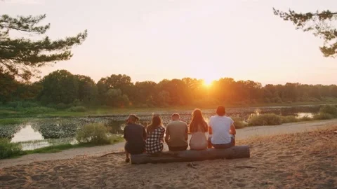 A group of young friends sit on a log by... | Stock Video | Pond5