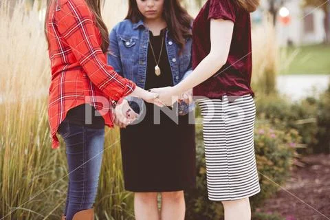 Group of young women holding hands and praying together in the park ...