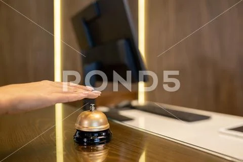 Photograph: Hand of young woman over bell on wooden counter going to ...