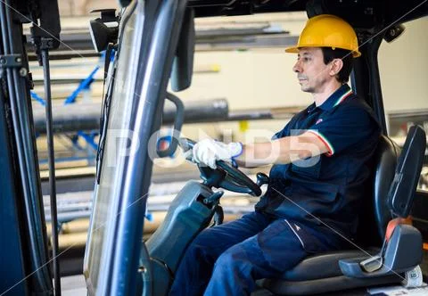 A handsome construction worker driving a forklift in an industrial ...