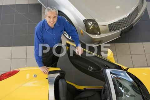 Photograph: Hispanic car salesman getting into new car #11611277