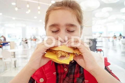 Hungry teenage girl eating a cheeseburger on the food court of the mall ...