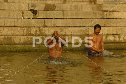 Indian man bathing and making offerings at the Ganges River in Varanasi ...