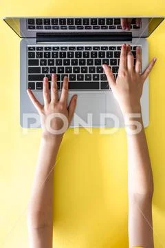 Kid hands typing on laptop computer keyboard on a yellow background ...