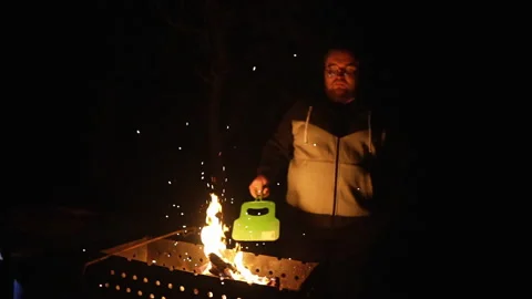 Large man kindling a fire in the brazier | Stock Video | Pond5