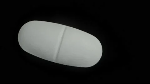 A large white pill rotates on a black ba... | Stock Video | Pond5