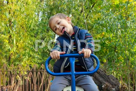 Photograph: Laughing little boy riding on a swing and looking at camera ...
