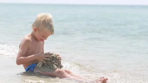 Little blonde boy playing with sand on b... | Stock Video | Pond5