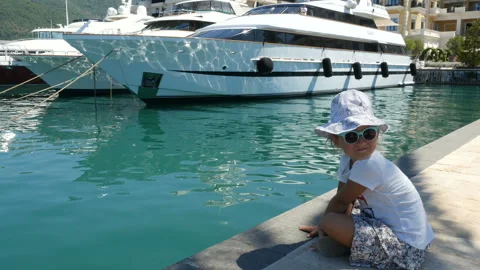 Little girl, kid sits on dock at seaport... | Stock Video | Pond5