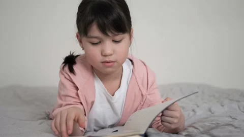 Little girl laying on the bed reading bo... | Stock Video | Pond5